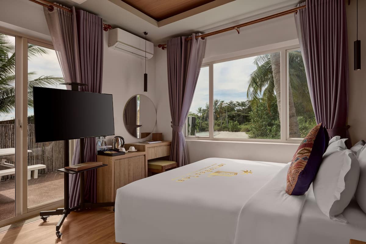 Quarto de hotel com cama, televisão, escrivaninha e janela com cortinas.