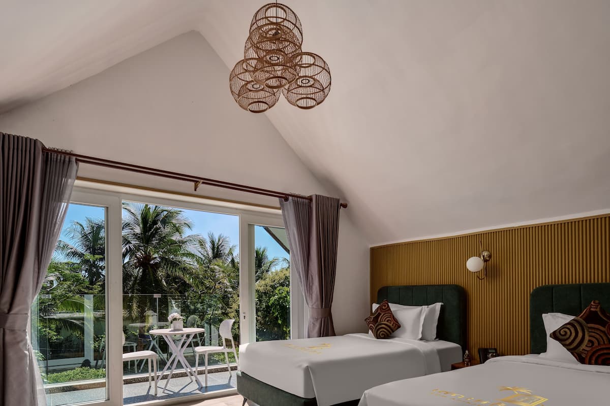 Quarto de hotel com duas camas, uma varanda com mesa e cadeiras, e vista para palmeiras.