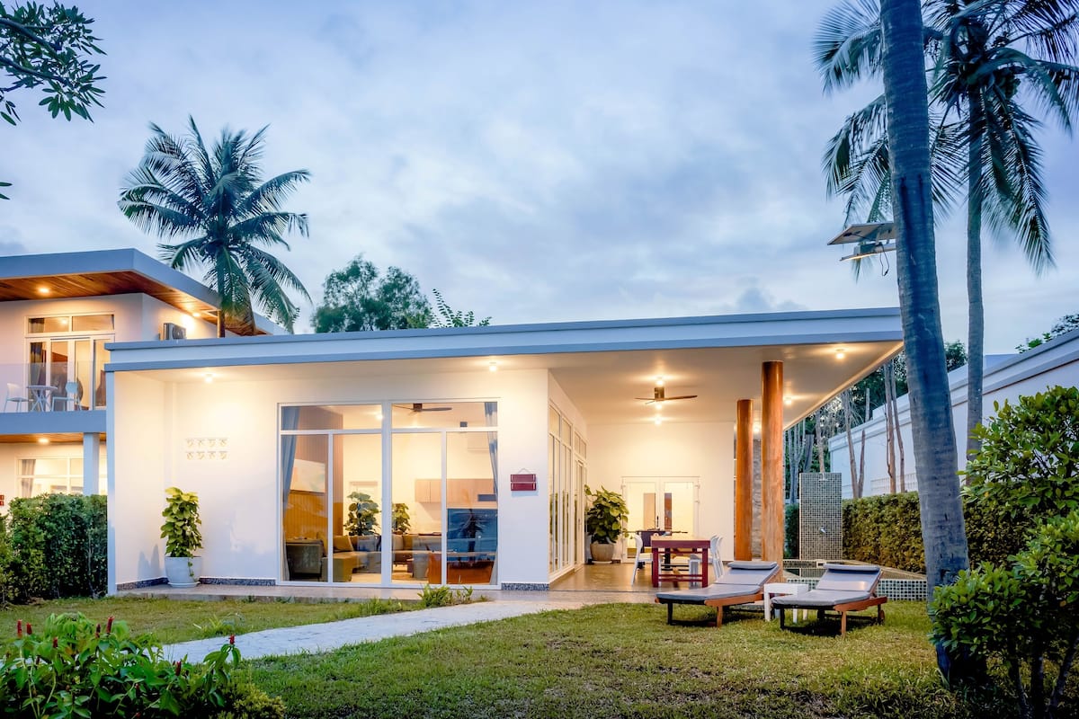 Uma casa moderna de dois andares com varanda coberta, portas de vidro e área de piscina.