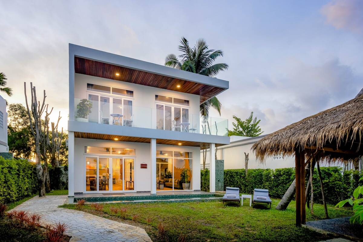 Uma casa moderna de dois andares com entrada de vidro, piscina e estrutura de telhado de palha.