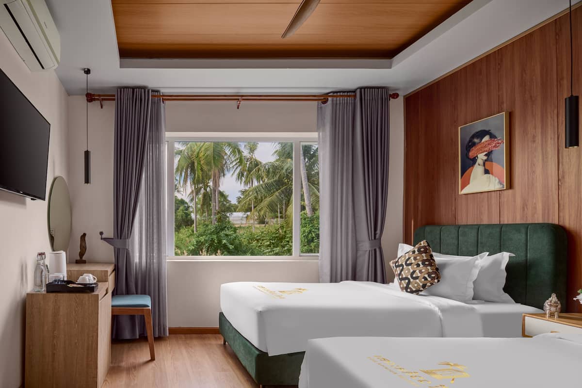 Quarto de hotel com duas camas, uma escrivaninha de madeira, televisão e janela com cortinas.