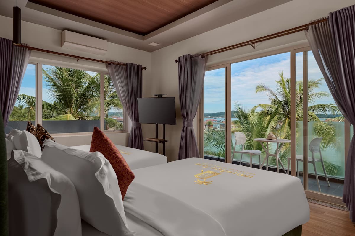 Quarto de hotel com duas camas, televisão e varanda com vista para palmeiras.