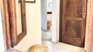 Uma porta de madeira com maçaneta de latão, uma cesta de palha no chão e um quadro na parede.