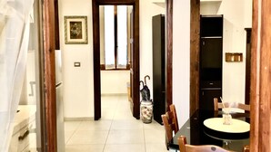Uma sala de jantar com mesa e cadeiras de madeira, um vaso e um quadro na parede.