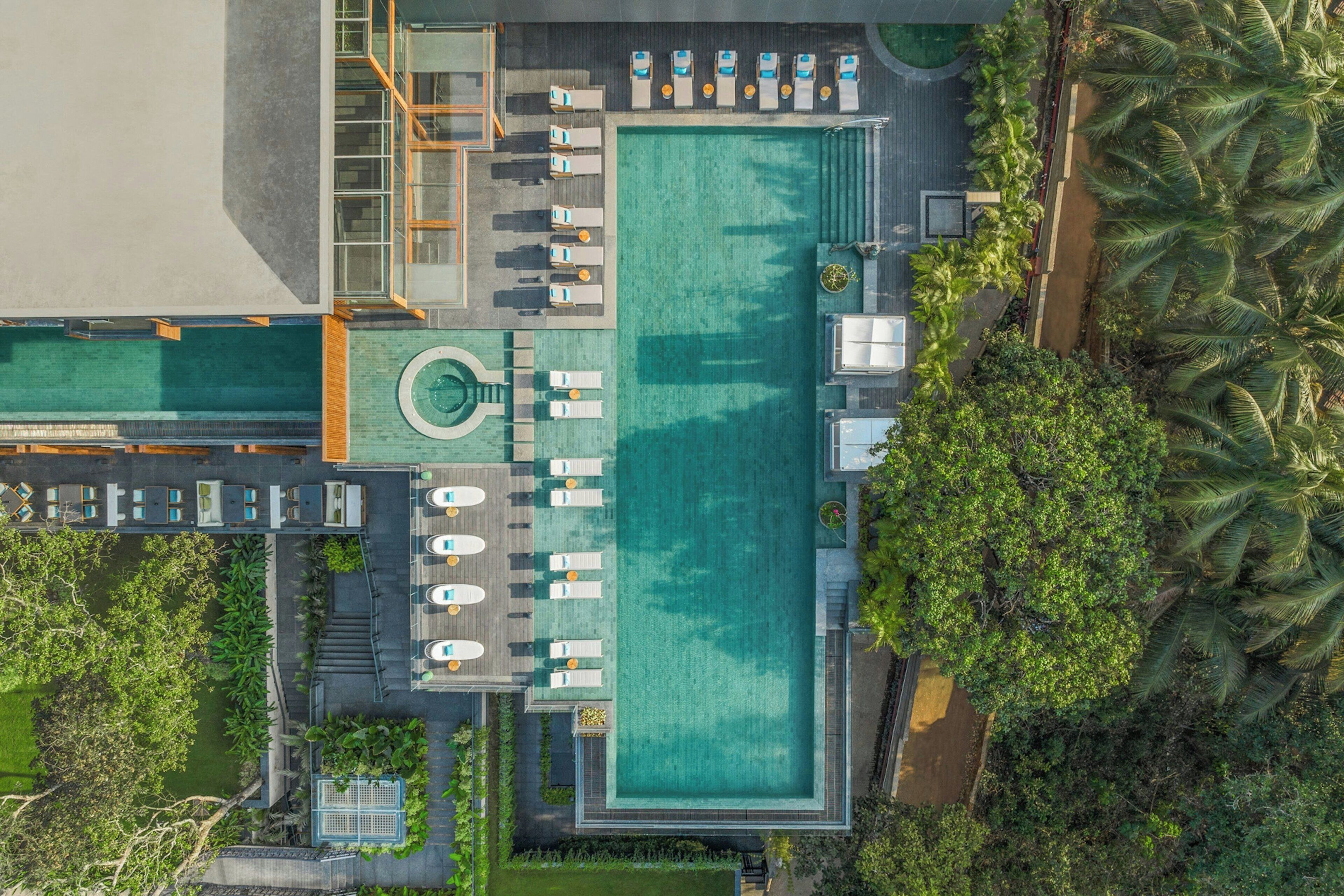 Vista aérea de um hotel com uma grande piscina, espreguiçadeiras e área com palmeiras.