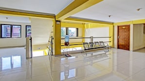 Um hall amplo e bem iluminado, com esquema de cores amarelo e branco, um balcão de recepção e uma área de espera com cadeiras.