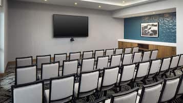 Uma sala de conferências com fileiras de cadeiras, uma TV de tela plana grande, um balcão de madeira e um painel decorativo.