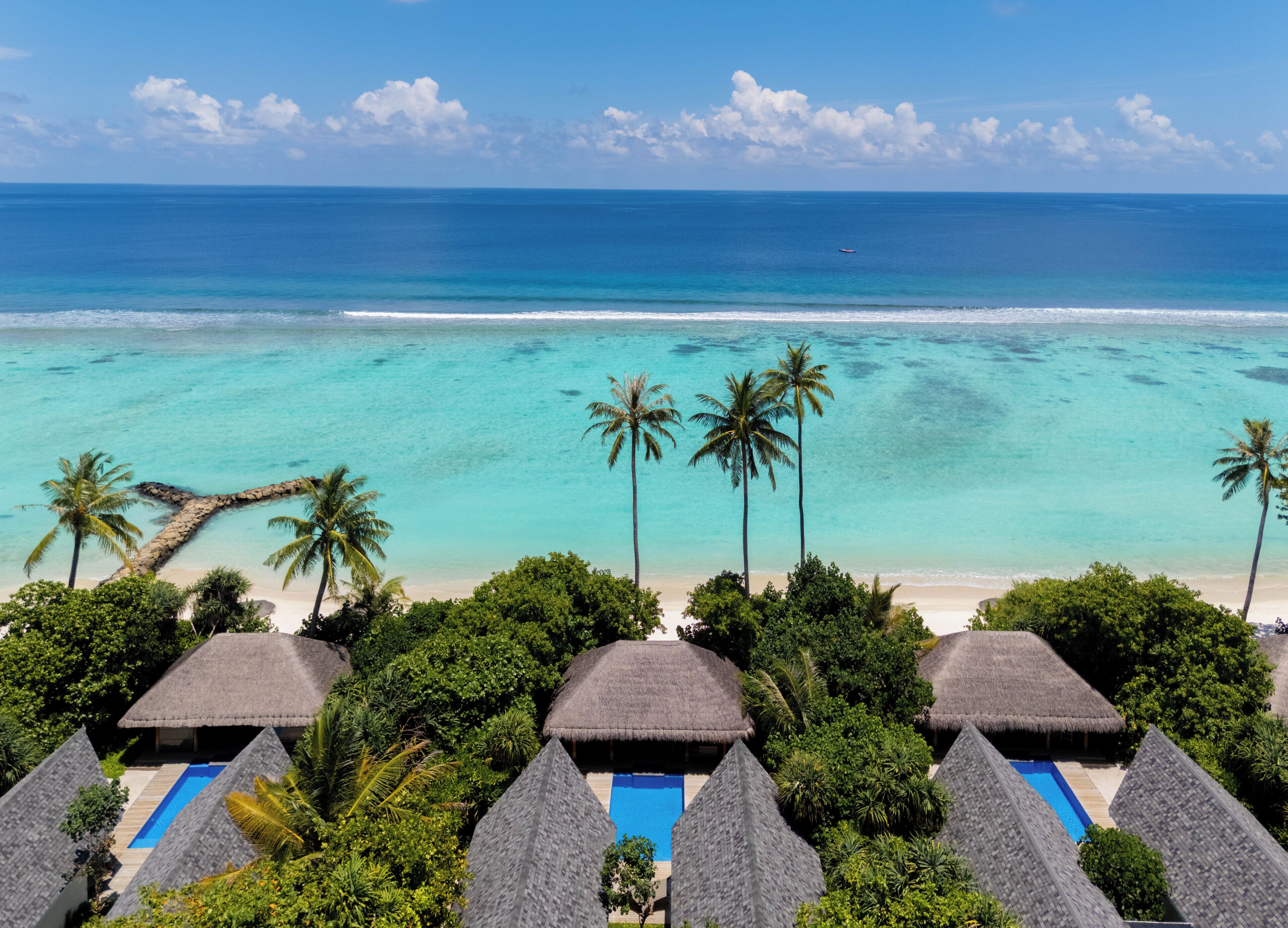 Um resort com bangalôs de telhado de palha, piscina e vista para o oceano.
