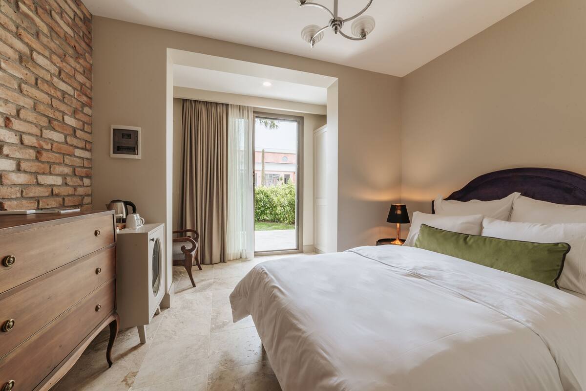 Quarto de hotel com cama, cômoda, luminária e vista para o exterior.