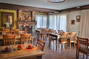 Uma sala de jantar com mesas e cadeiras de madeira, uma lareira de tijolos e enfeites de Natal.