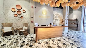 Uma área de recepção com um balcão de madeira, cadeiras de vime e piso estampado.