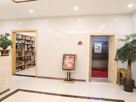 Um saguão de hotel com piso de azulejos, balcão de recepção, placa na parede e planta em vaso.