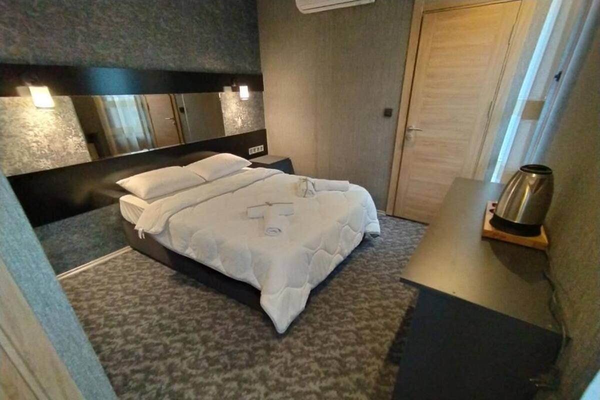 Quarto de hotel com uma cama, mesa de cabeceira, espelho e porta.