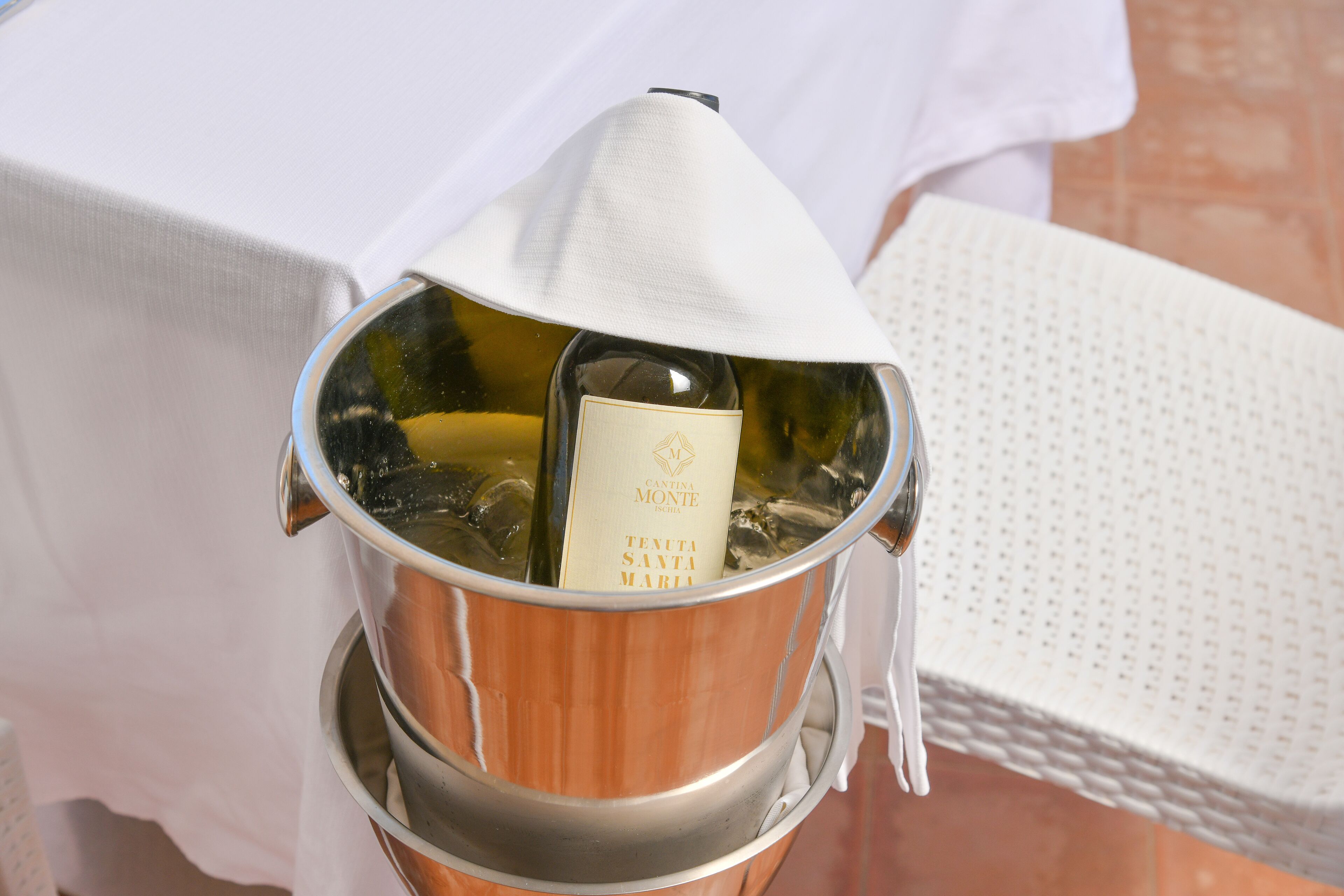 Um balde de cobre com uma garrafa de vinho, um tecido branco e uma toalha de mesa branca.