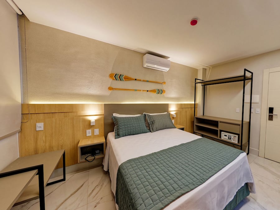 Quarto de hotel com cama, mesas de cabeceira, ar condicionado fixado na parede e televisão.