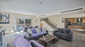 Uma sala de estar ampla com um conjunto de sofás, uma mesa de centro e uma escada que leva ao andar superior.