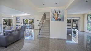 Ampla sala de estar com design moderno, incluindo uma escadaria, uma pintura grande e um espaço de estar com sofá e poltronas.