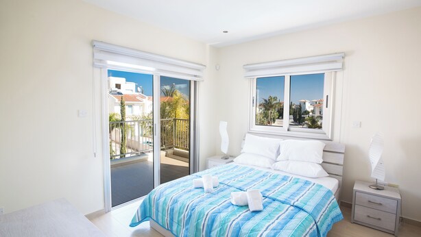 Quarto com cama, mesa de cabeceira, abajur e vista para o exterior.
