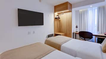 Quarto de hotel com duas camas, uma escrivaninha, uma cadeira, televisão e janela com cortinas.