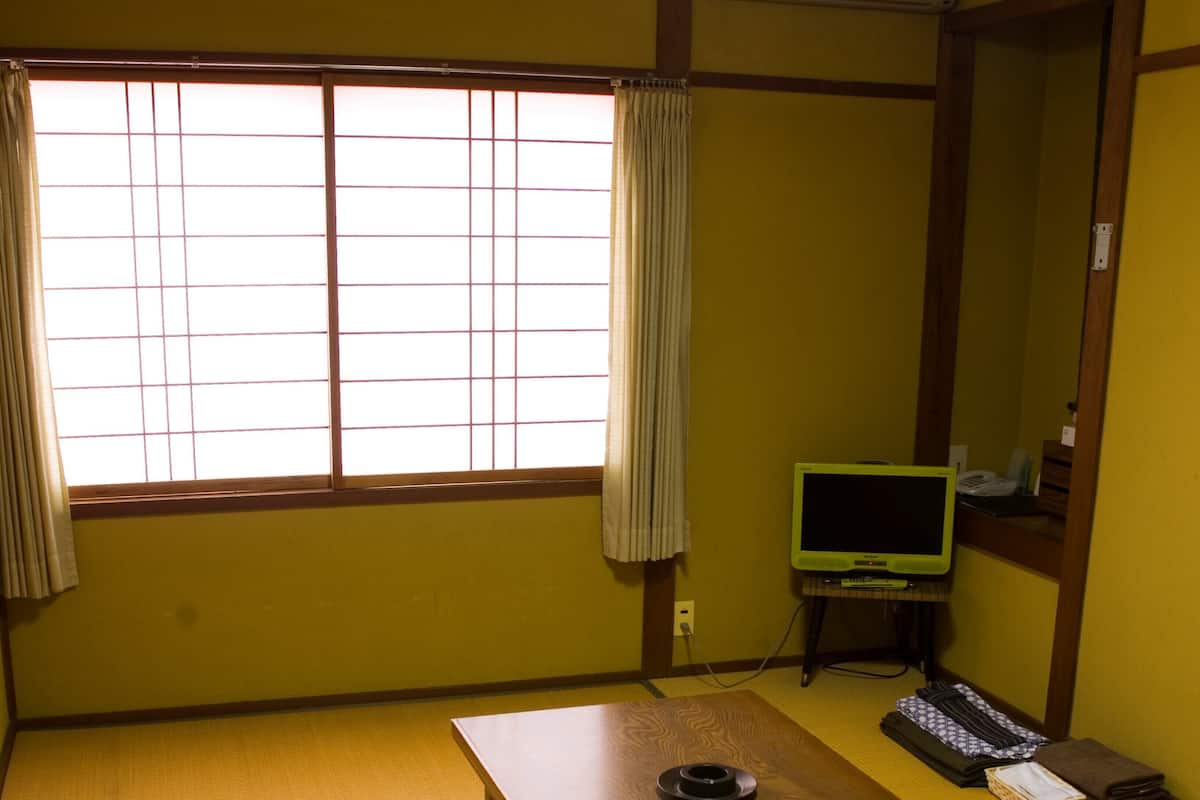 Quarto japonês tradicional com tatames, uma mesa de madeira baixa, uma televisão e uma escrivaninha com teclado.