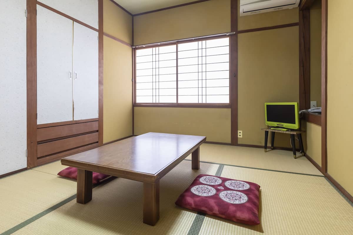 Um quarto japonês tradicional com tatames, uma mesa de madeira baixa, uma TV sobre um pequeno suporte e uma porta deslizante.