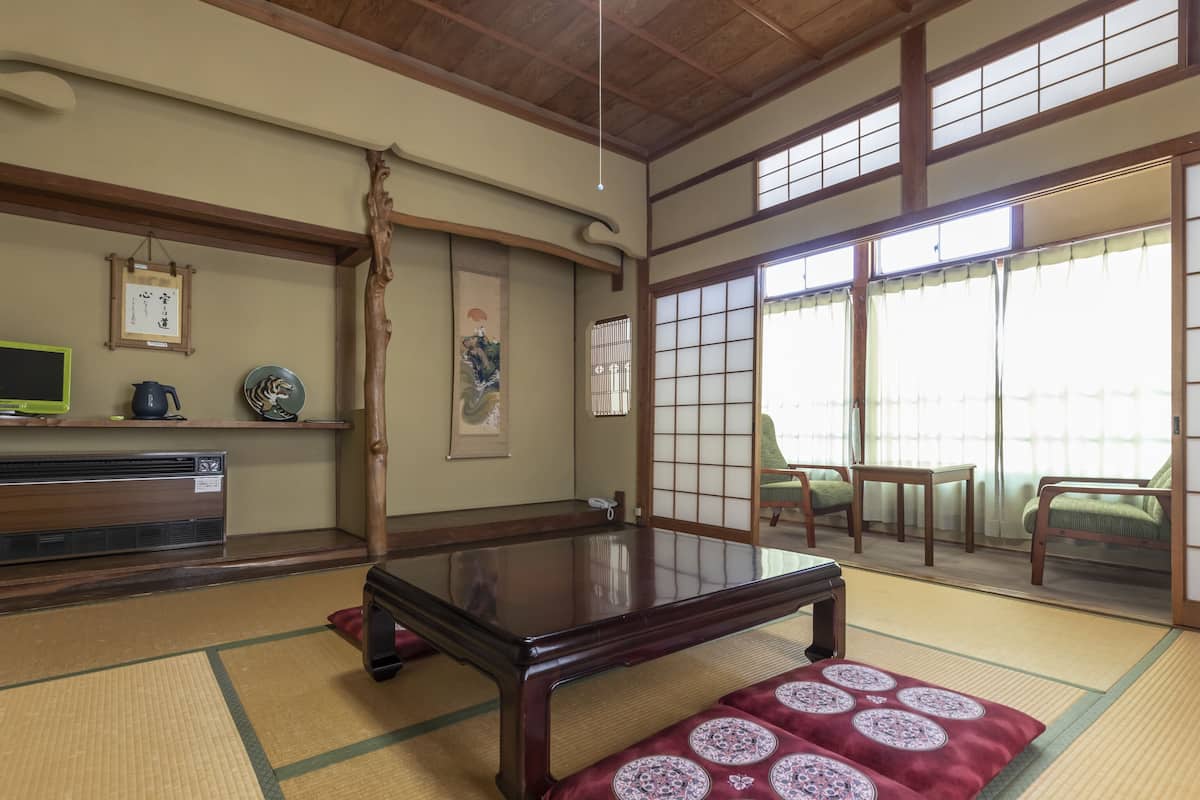 Um quarto japonês tradicional com piso de tatame, uma mesa de madeira baixa, portas deslizantes shoji e uma cadeira verde.