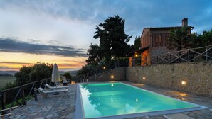 Piscina com piso de pedra, espreguiçadeiras e uma parede de pedra.