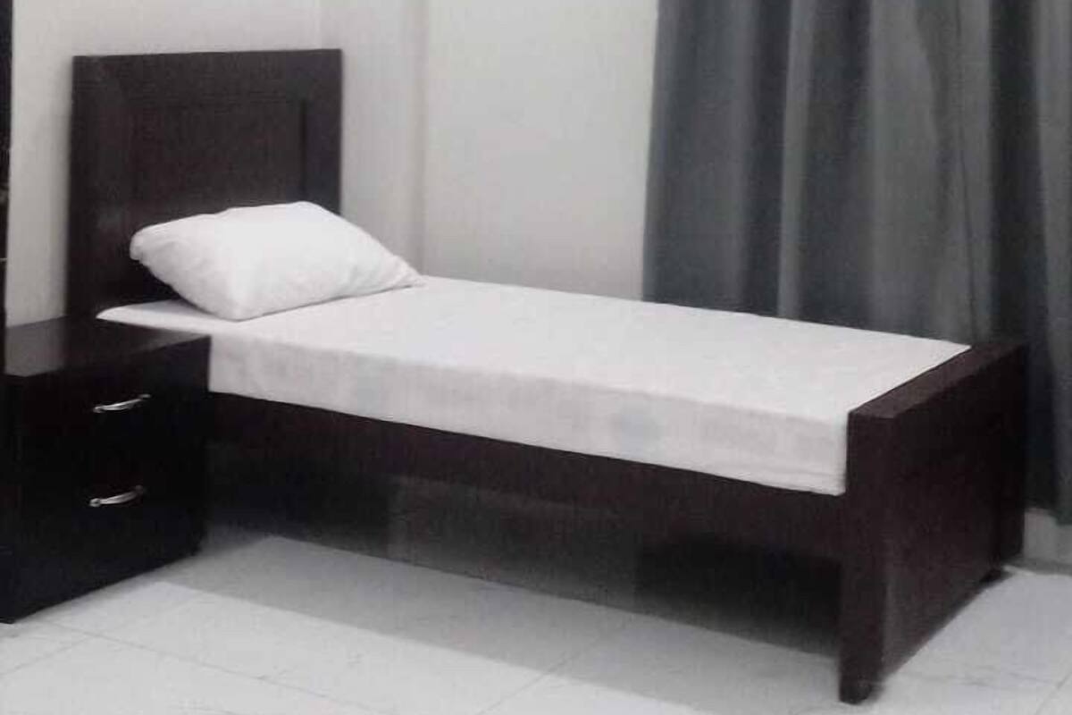 Quarto com uma cama de solteiro, mesa de cabeceira, ventoinha no teto e janela com cortinas.