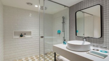 Casa de banho moderna com cabine de duche em vidro, lavatório branco com cuba redonda e espelho com moldura preta.