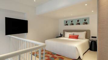 Quarto de hotel moderno com uma cama grande, televisão de tela plana na parede, uma mesinha de cabeceira e um tapete colorido.