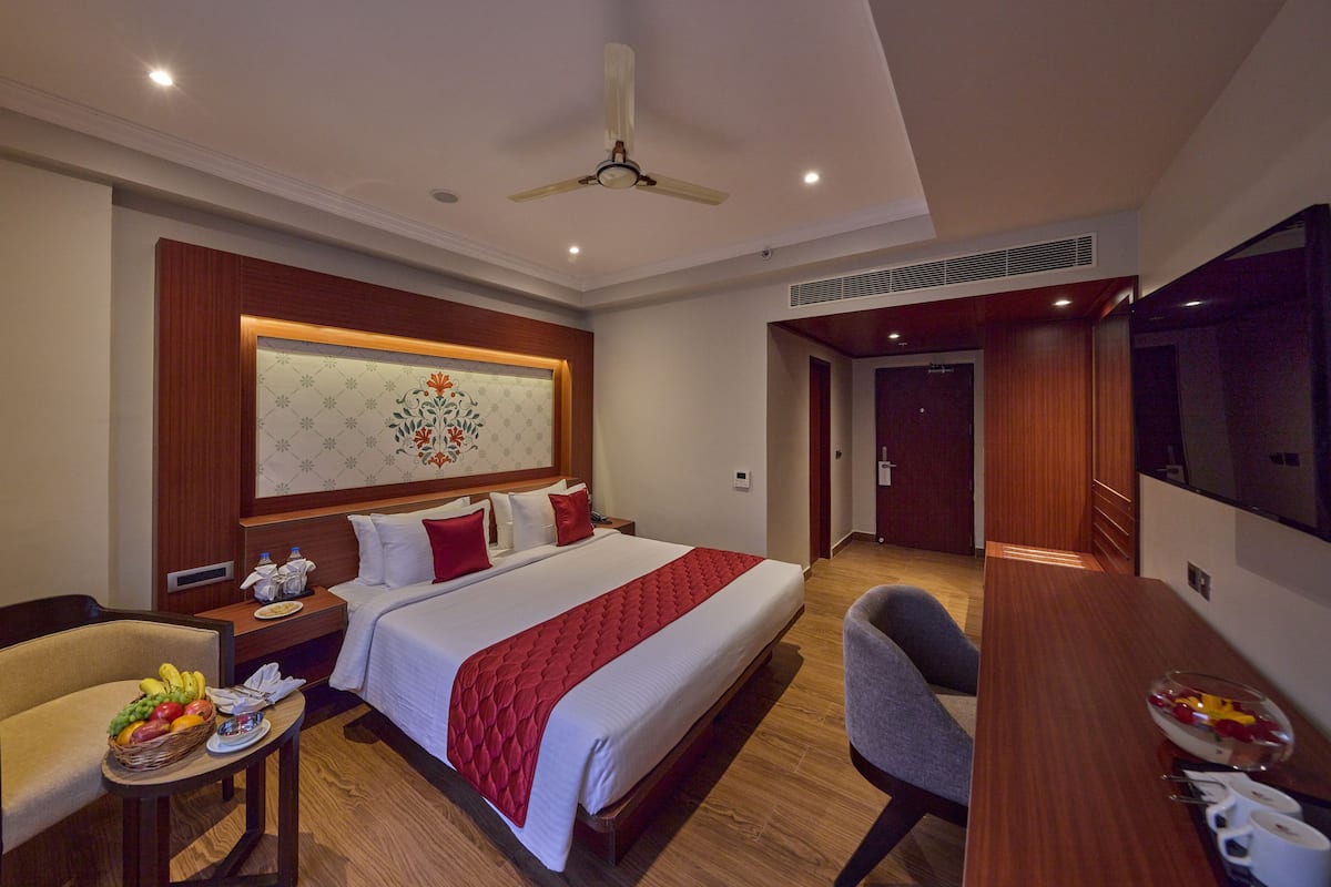 Quarto de hotel com uma cama grande, uma escrivaninha, uma cadeira, uma TV e uma cesta de frutas.