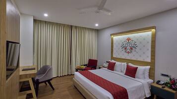 Quarto de hotel com cama, escrivaninha, cadeira, mesa de cabeceira e uma obra de arte na parede.