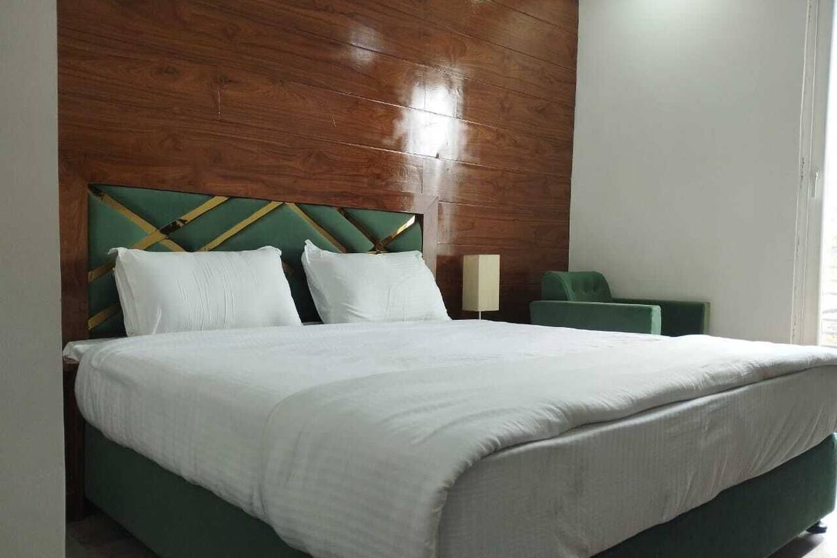 Cama bem arrumada com cabeceira estofada verde e roupa de cama branca.