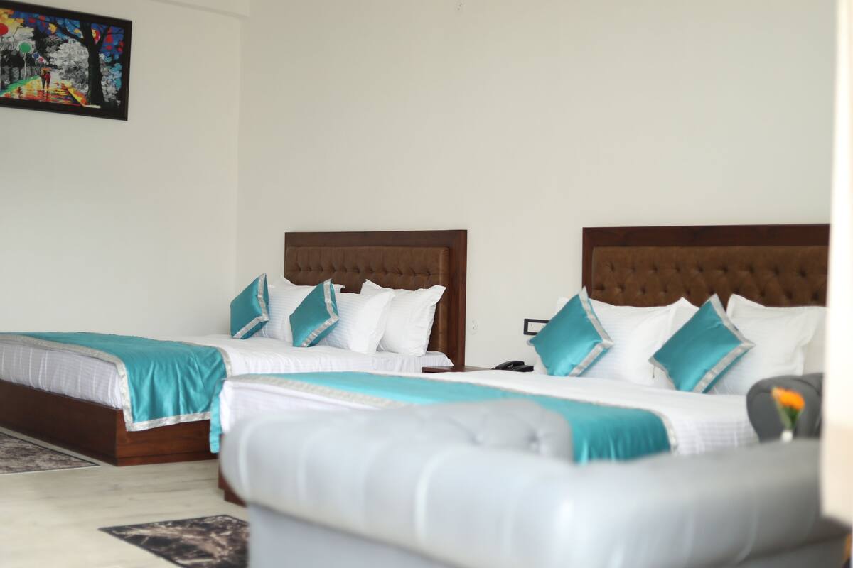 Quarto de hotel com duas camas, cada uma com cabeceira de madeira, roupa de cama branca e detalhes em verde-água.