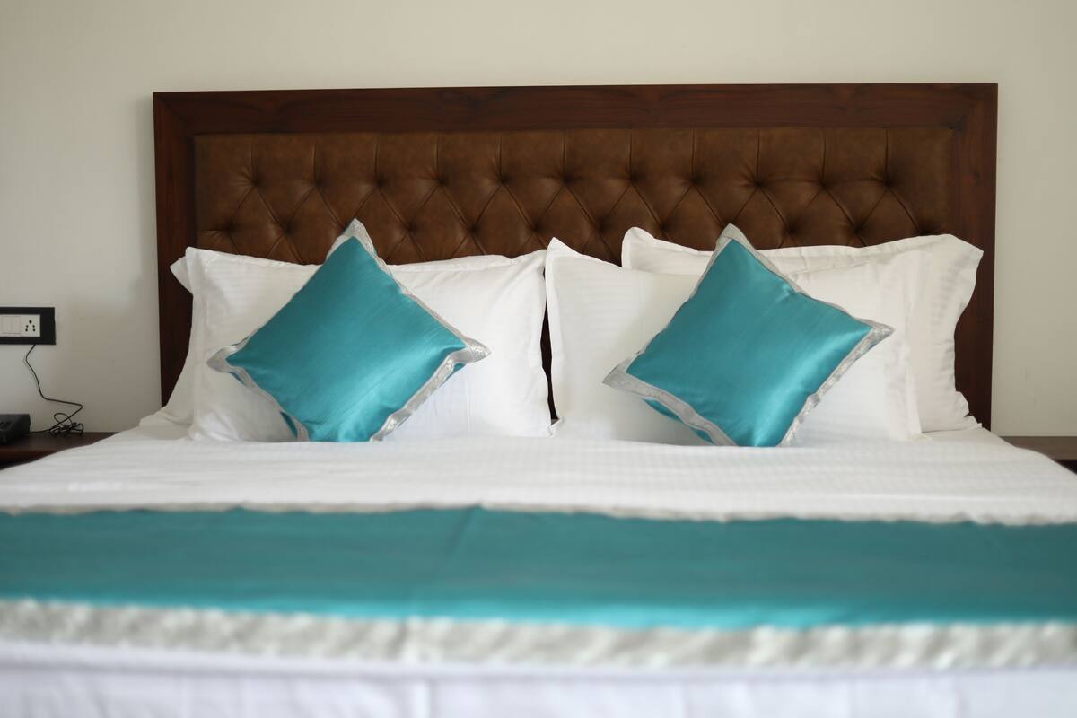 Cama bem arrumada com cabeceira estofada, roupa de cama branca e dois travesseiros verde-água.