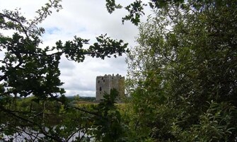 Uma torre de pedra histórica rodeada por vegetação densa e um corpo de água.