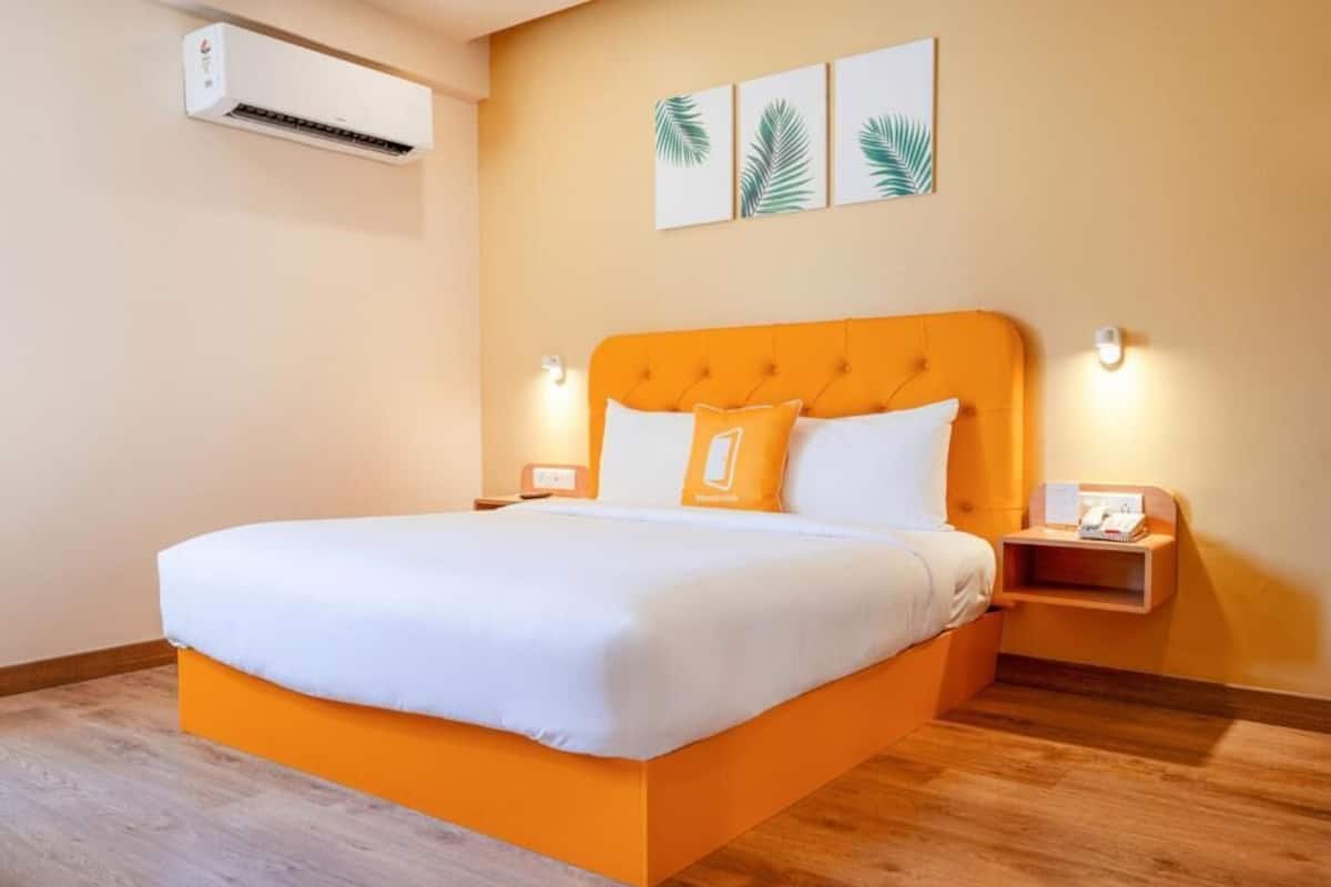 Quarto de hotel com uma cama, ar condicionado, mesa de cabeceira e prateleira na parede.