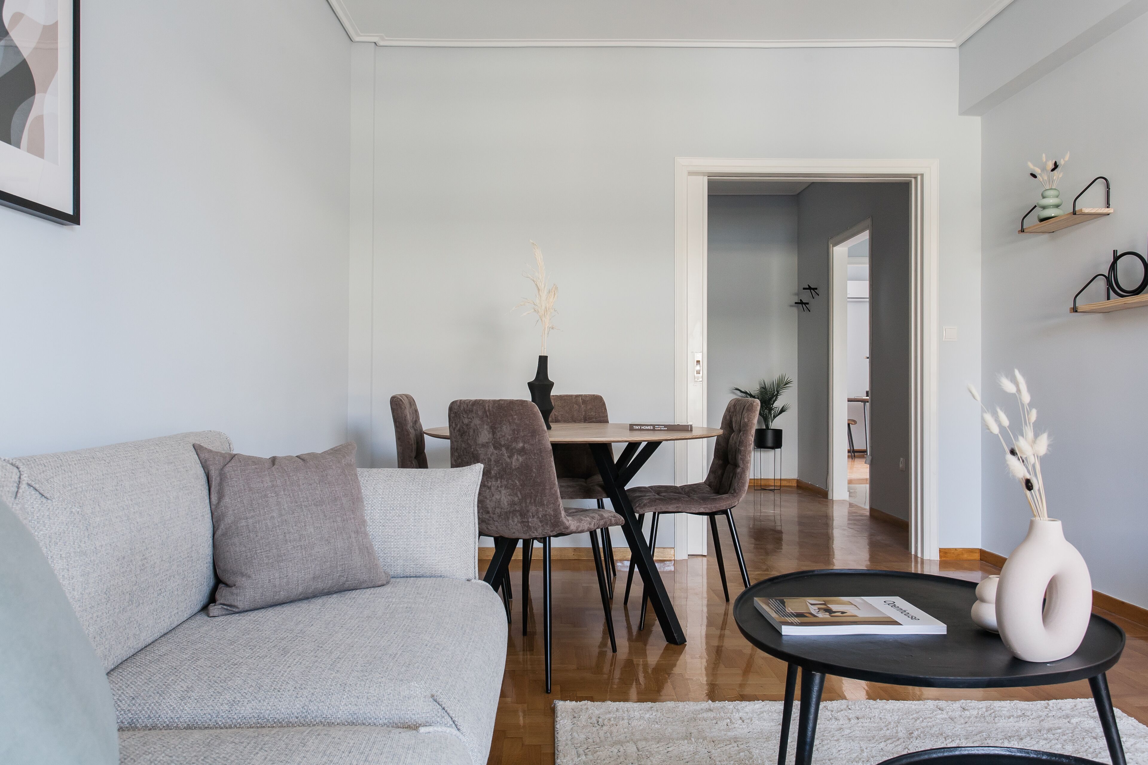 Uma sala de estar moderna com um sofá cinza, uma mesa de jantar com cadeiras e uma mesa de centro com um vaso.