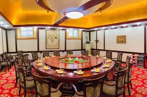 Sala de conferências com mesa redonda, cadeiras e piso coberto por um tapete vermelho.