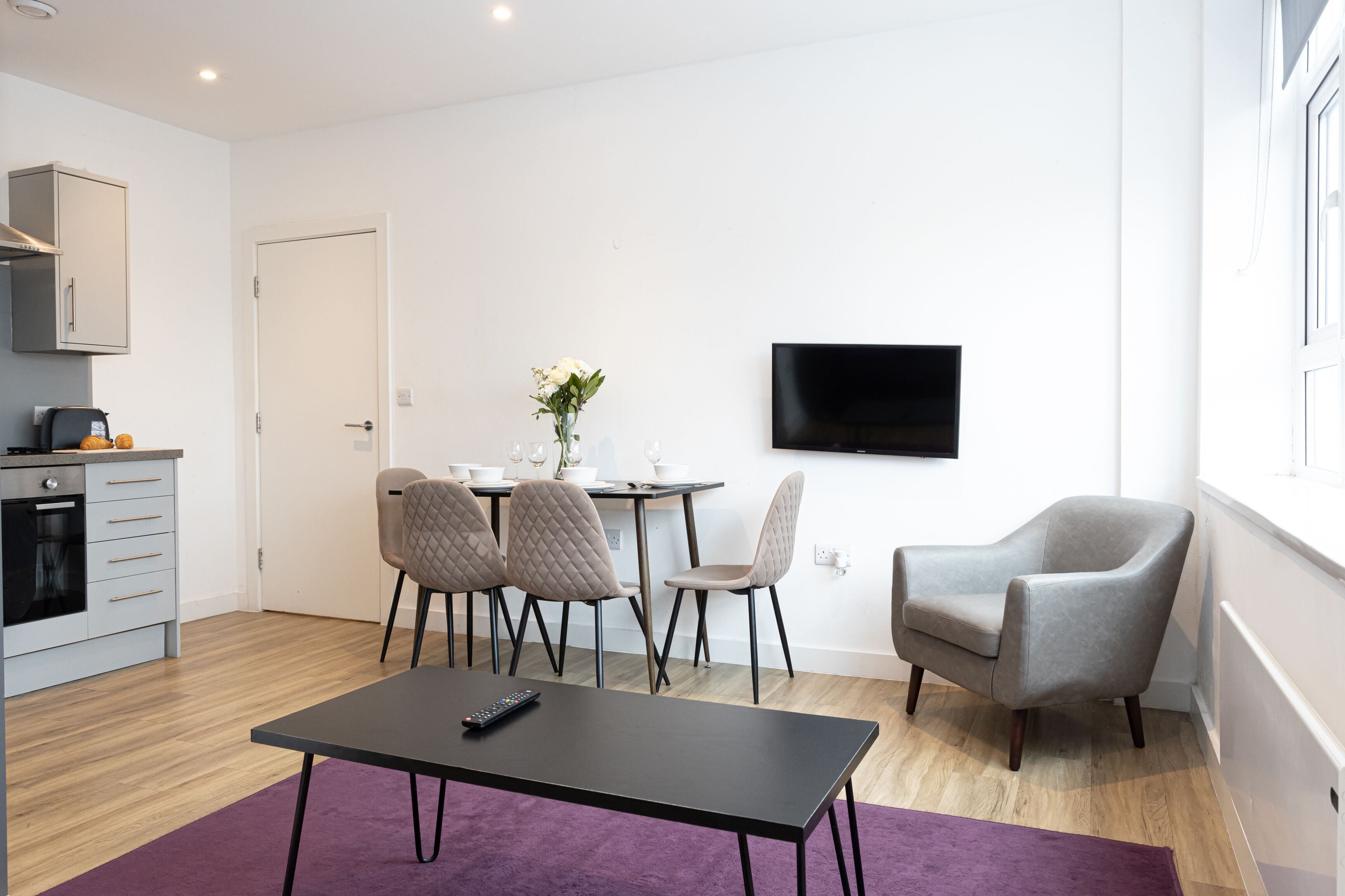 Uma sala de estar moderna com área de jantar, cozinha e televisão fixada na parede.