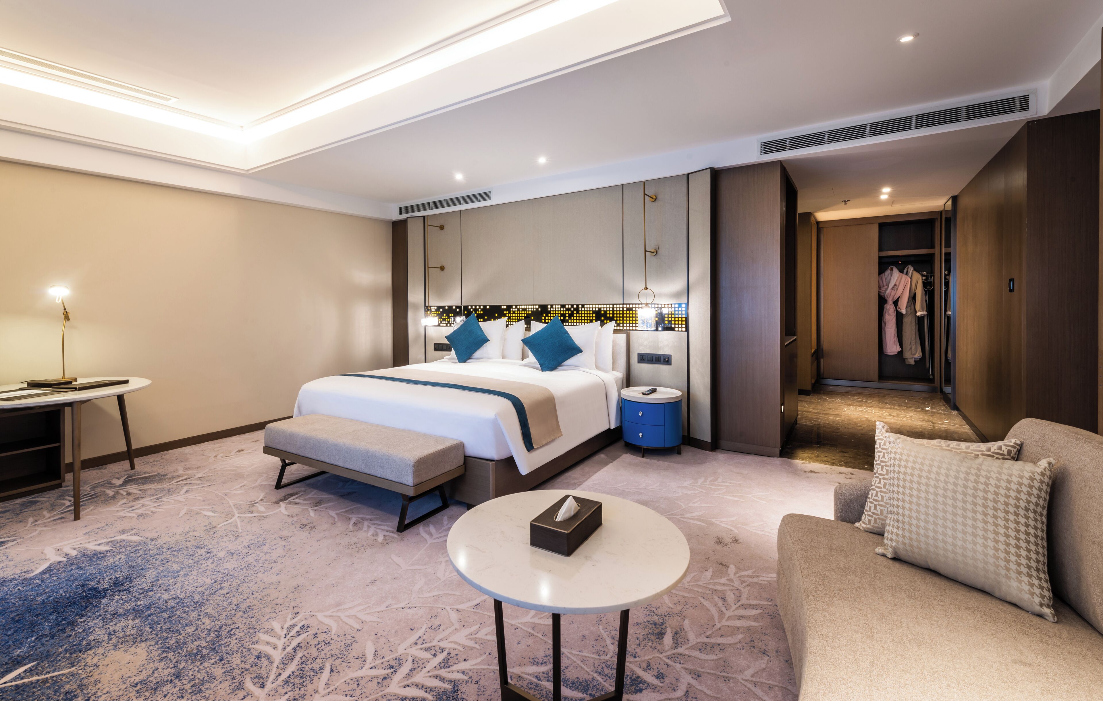 Quarto de hotel moderno com cama grande, mesas de cabeceira, área de estar e closet espaçoso.