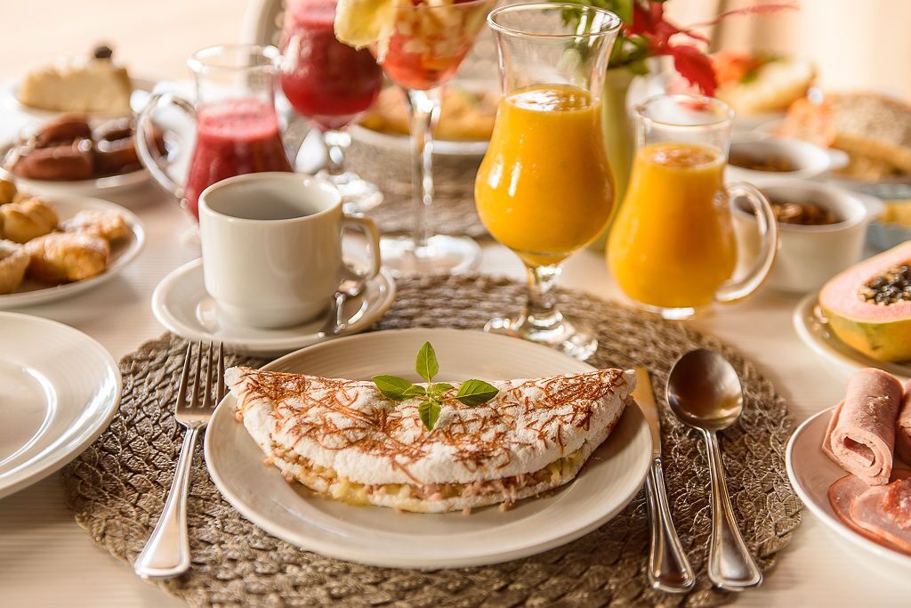 Uma mesa de café da manhã com crepes, uma xícara de café e um copo de suco de laranja.