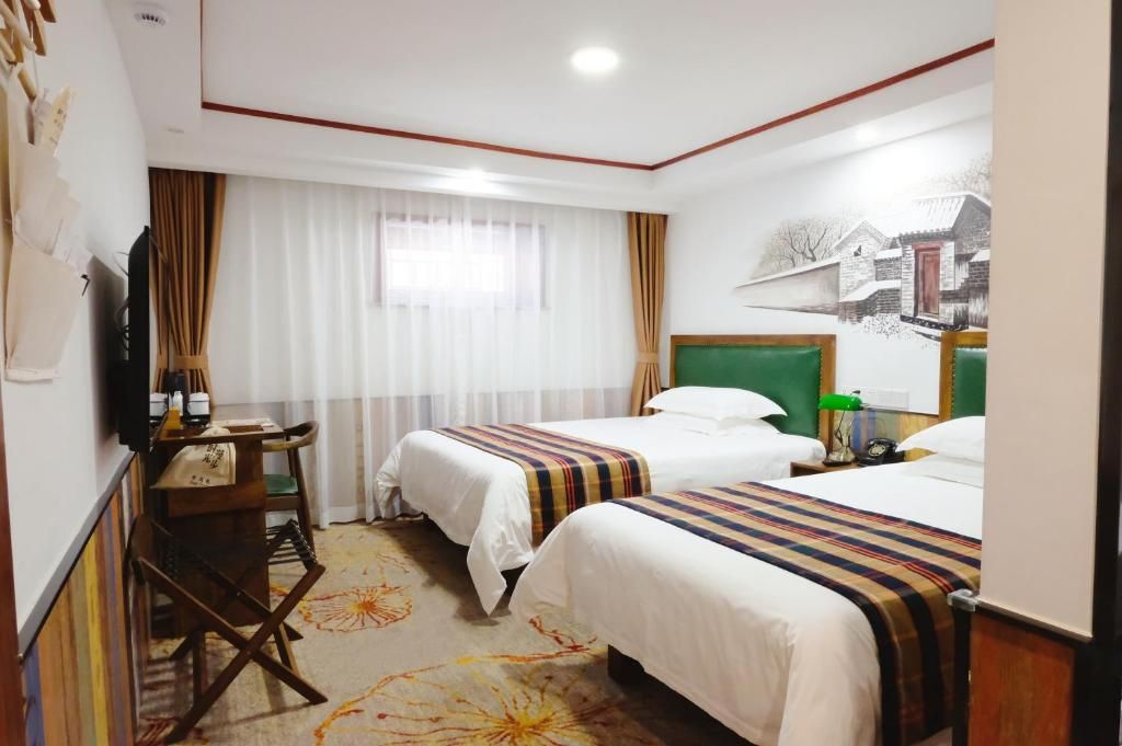 Quarto de hotel com duas camas, uma escrivaninha, televisão e janela com cortinas.