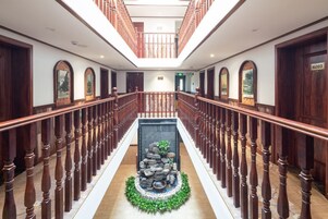 Um amplo hall de hotel com uma escadaria central, corrimãos de madeira e uma fonte decorativa.