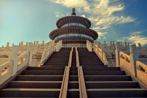 Uma imponente escadaria leva a um pavilhão tradicional chinês, com grades ornamentadas e céu claro acima.