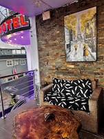 Um hall de hotel com parede de pedra, um sofá de vime, uma mesa de centro de madeira e uma pintura retratando uma cena de rua.