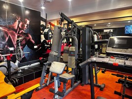 Uma academia com diversos equipamentos de exercício, incluindo um banco de supino, suporte para agachamento e esteira.