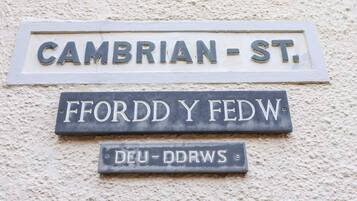 Uma placa de rua com o nome 'CAMBRIAN-ST.' e duas placas menores abaixo dela com as inscrições 'FFORDD Y FEDW' e 'DEU-DDRWS'.
