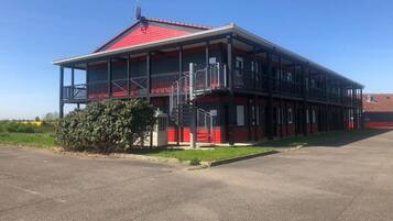 Um edifício de dois andares com varandas, telhado vermelho e céu claro.