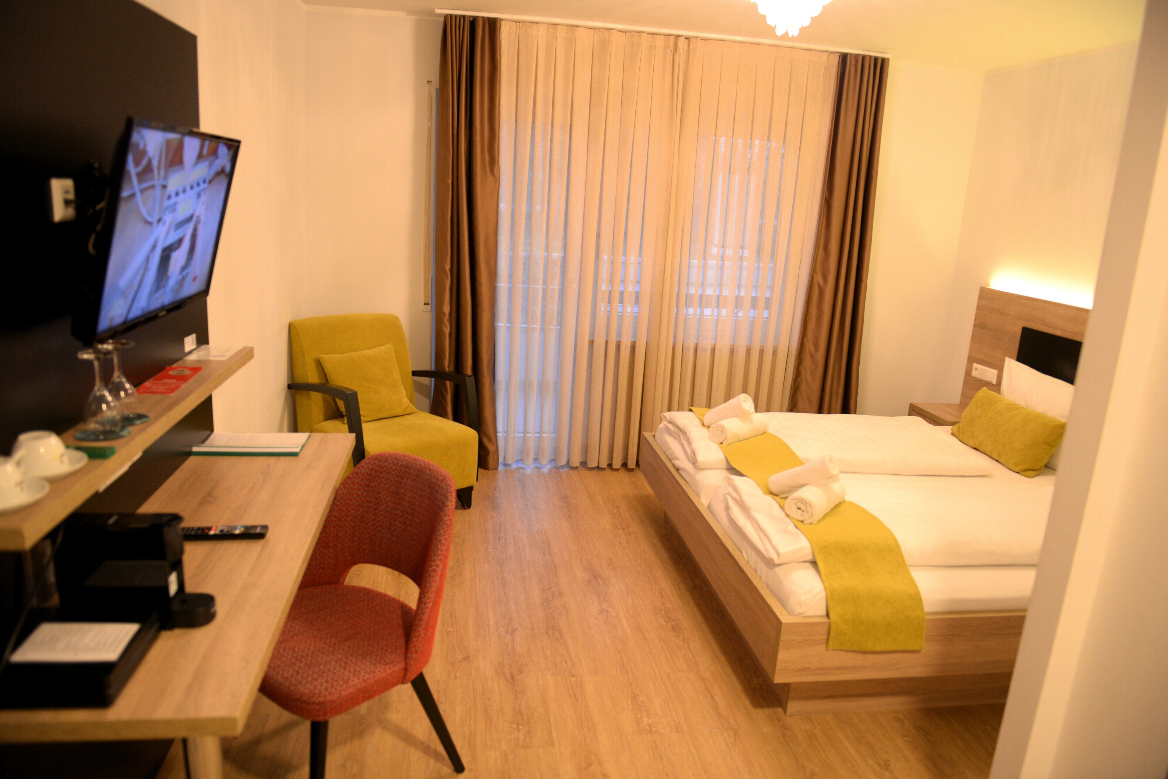 Quarto de hotel com secretária, duas cadeiras, cama e televisão.